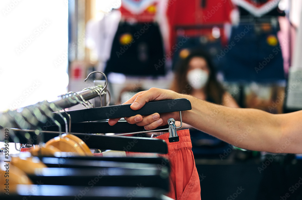 Detail of a man's hand holding a clothes hanger in a shop, with the ...