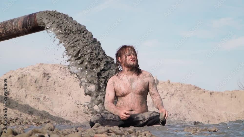 Funny Fat Man with Long Hair Sits in the Mud. Against the background ...