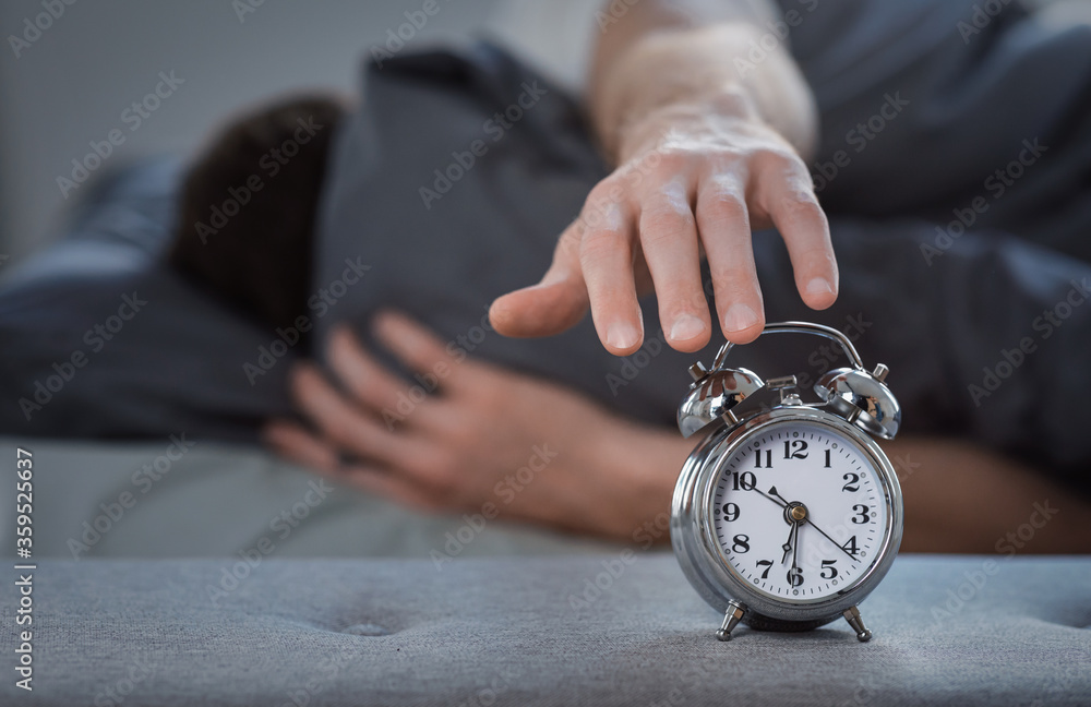 Man Turning Off Alarm-Clock Lying In Bed At Home Stock Photo | Adobe Stock