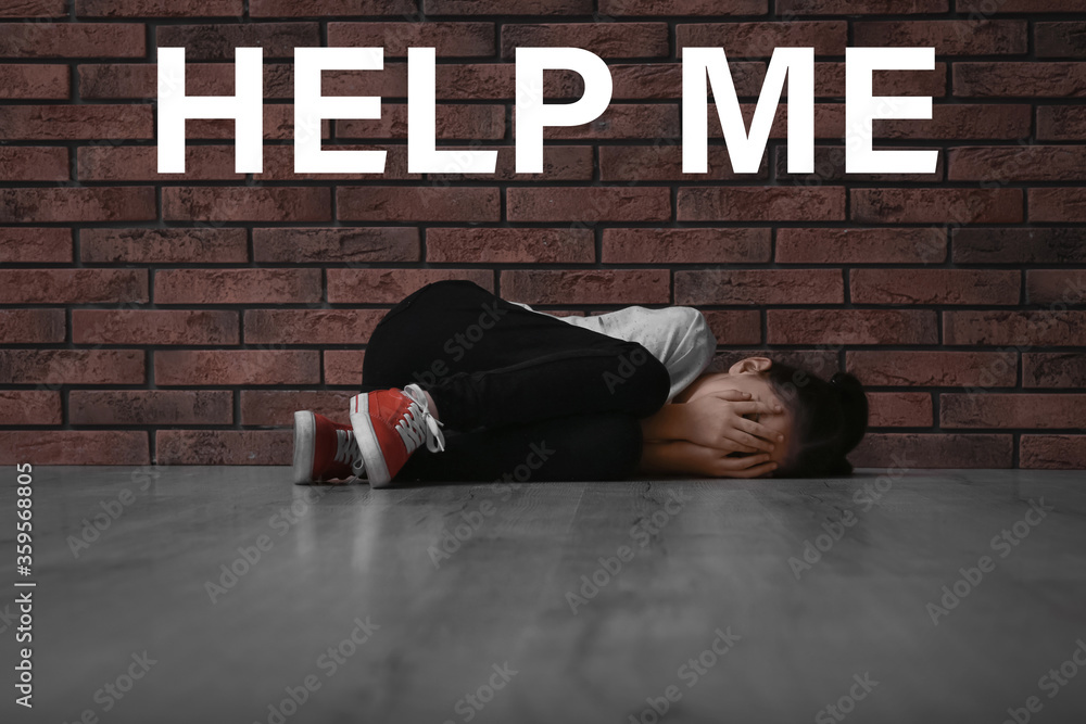 Scared little girl lying on floor near brick wall and text HELP ME ...