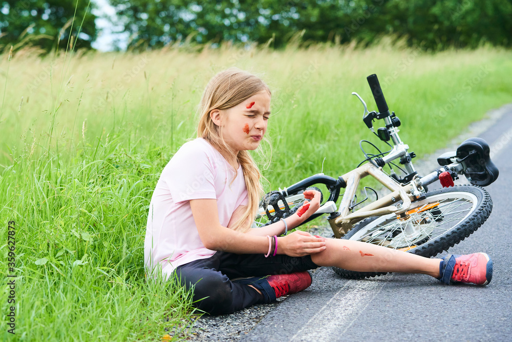 Sad crying little child girl fell from the bike in the summer park ...