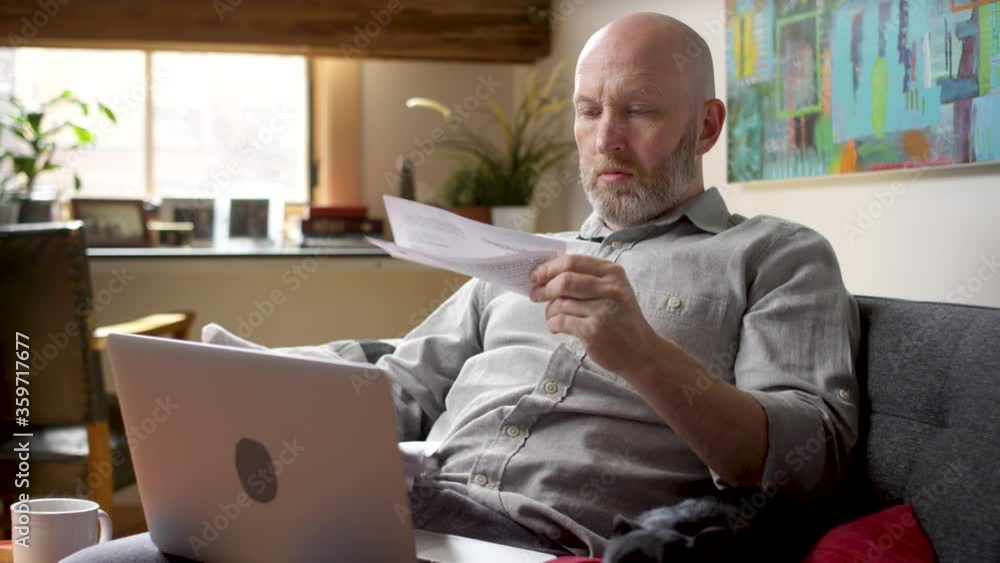 Man looking through his stack of mail, opens up an envelope with a bill ...