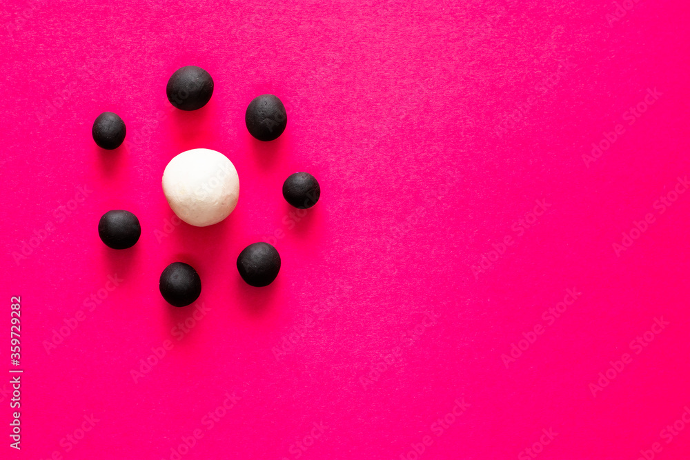 Small black balls surrounding a large white plasticine ball on pink ...