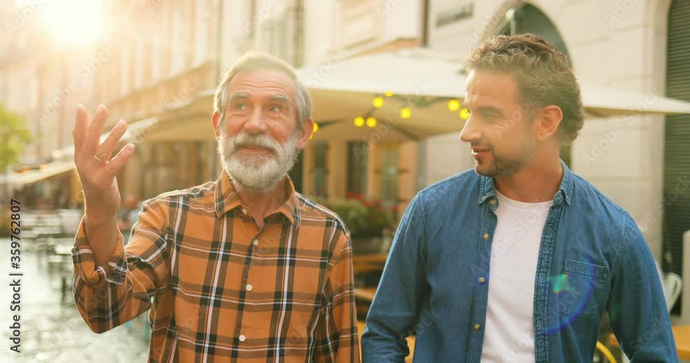 Two male generations walking the street in town and talking. Father and ...