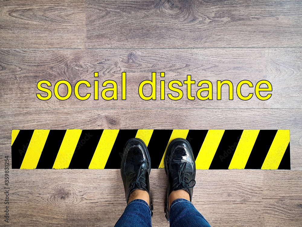 person stands in line with yellow and black stripes keeping safe social ...