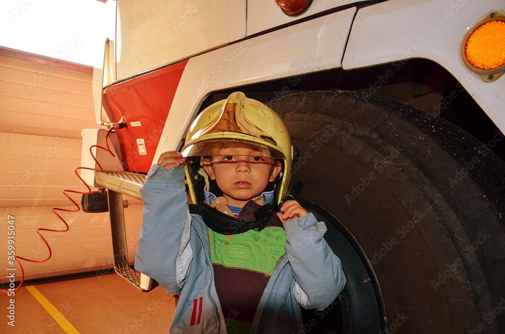Little boy acting like a fireman. Boy standing next a real fireman car ...