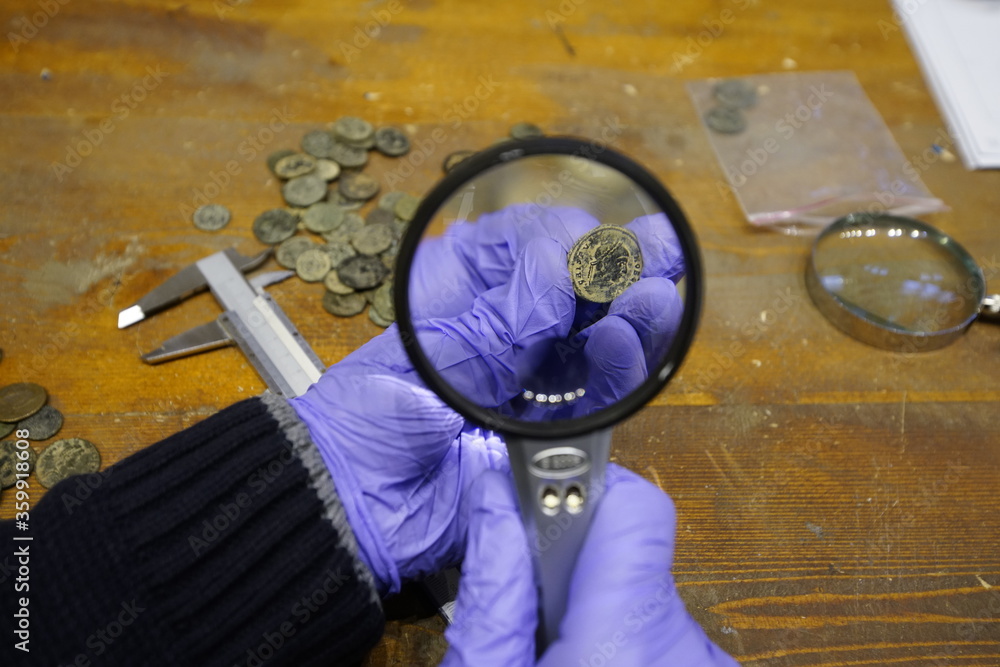 archaeologist checking coins with a magnifying glass. archeology ...