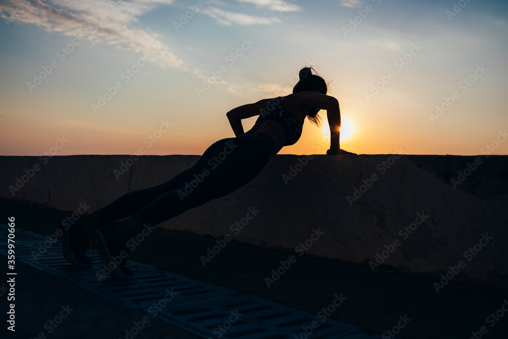 Full length of silhouette female athlete doing push-ups at promenade ...