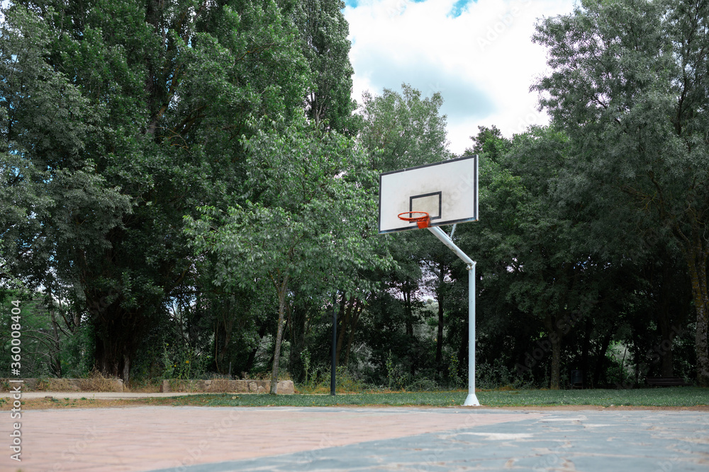 basketball court in a park with trees with white board and no net on ...