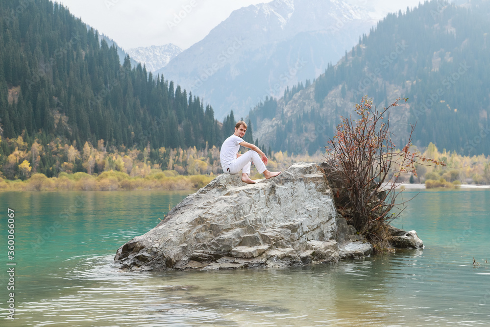 Handsome male model in white clothes sitting on rock a background of ...