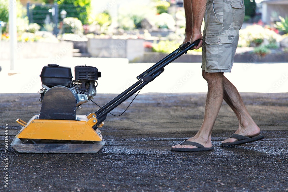 male Worker using vibratory plate compactor to firm soil at worksite ...