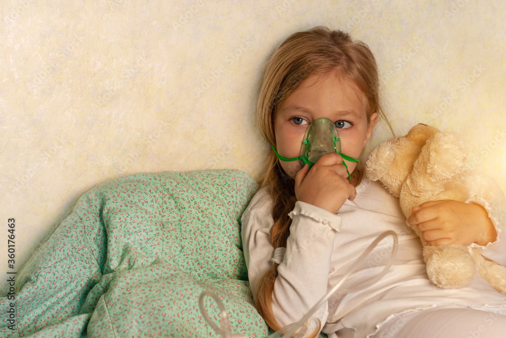 Little girl making inhalation with nebulizer on a bed at home. Sick ...