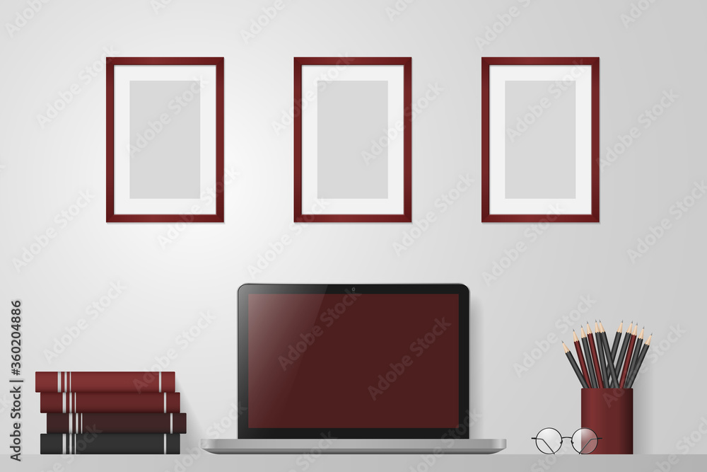 Workspace with laptop, empty frames, books and pencils on white wall ...