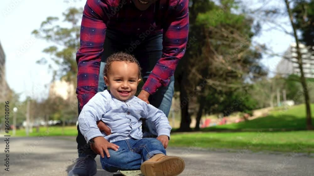 African American bald father holding son on skateboard in park. Cute ...