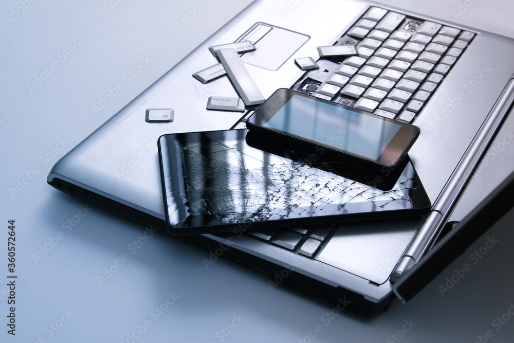 A silver laptop with a broken keyboard, tablet with a cracked display ...