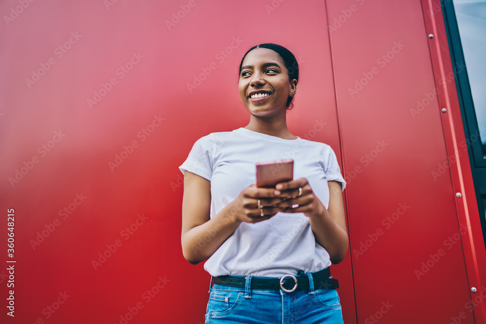 Smiling young African American woman in t-shirt holding mobile phone ...