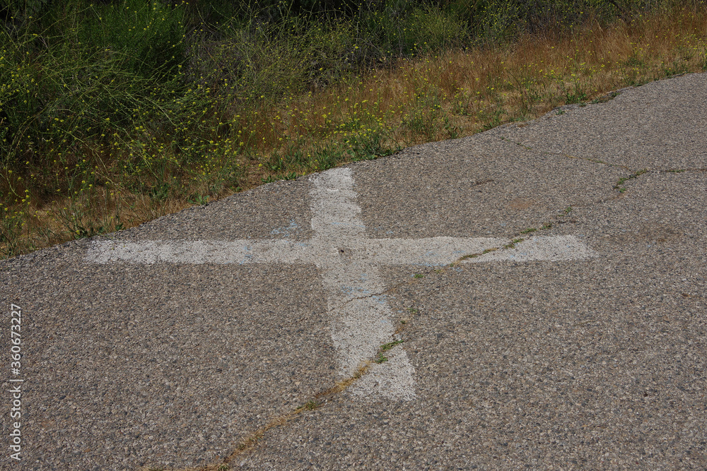 A large white cross sign on the pavement of an old country road with a ...