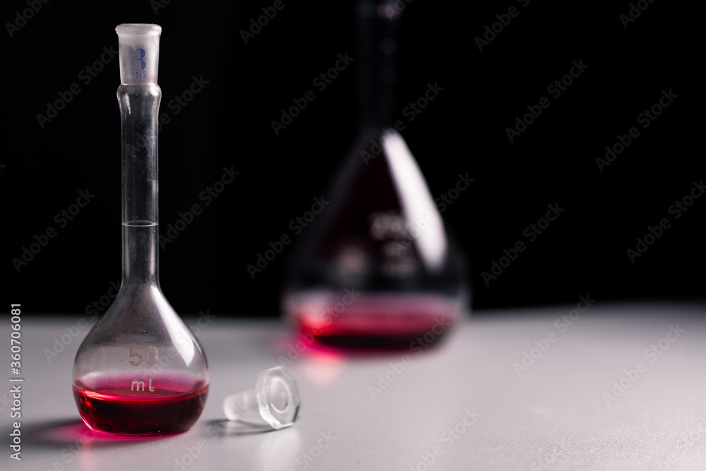 closeup of two conical erlenmeyer flasks with red liquid and a glass ...