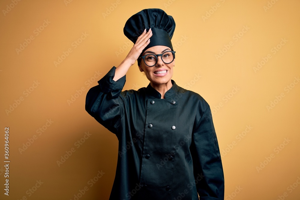 Young beautiful brunette chef woman wearing cooker uniform and hat over ...