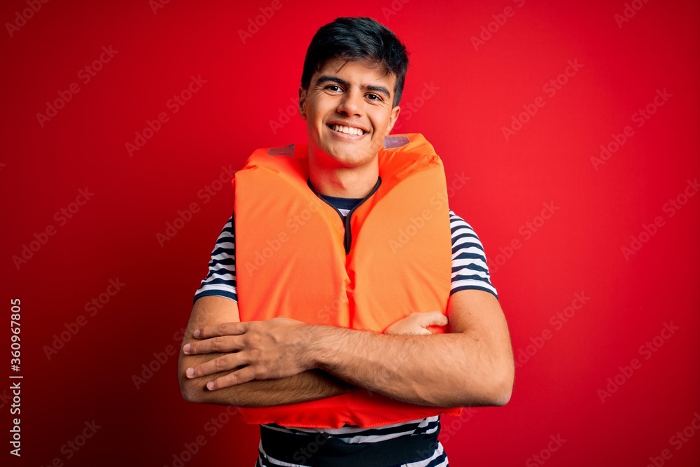 Young handsome man wearing orange safety life jacket over isolated red ...