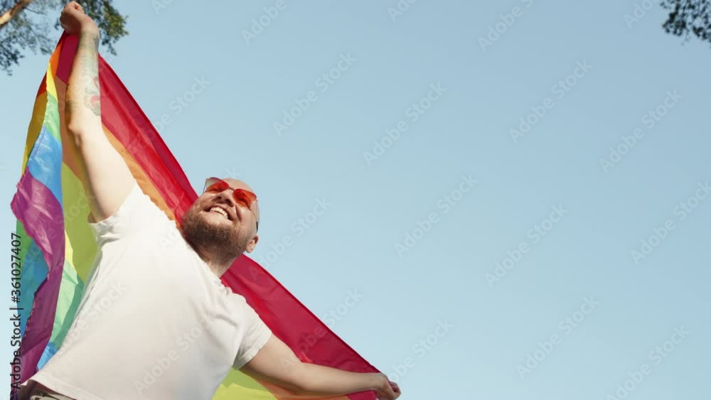 Homosexual man holding rainbow gay flag while parade on background of ...
