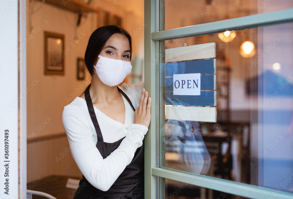 Young waitress with face mask by entrance door in cafe, reopening ...