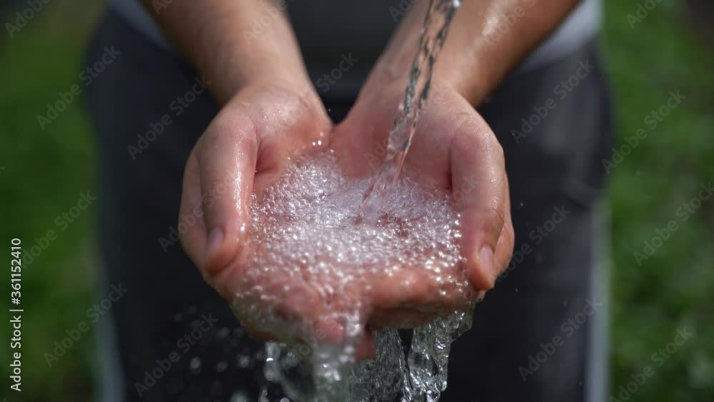 stream of fresh drinking water pouring into human hands, dry farmland ...