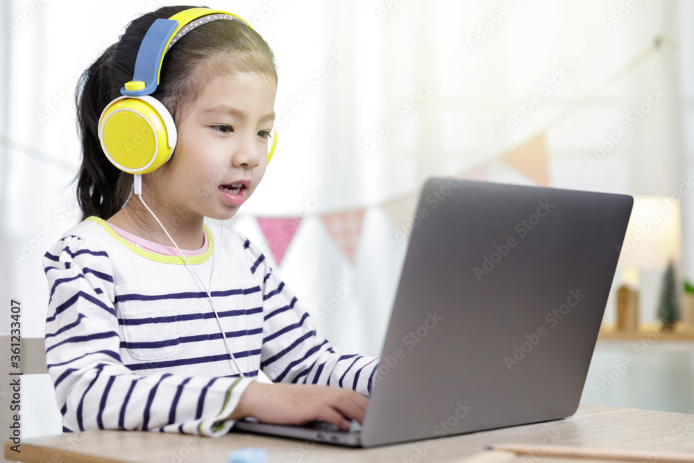 Asian little child girl learning at home with laptop computer using ...