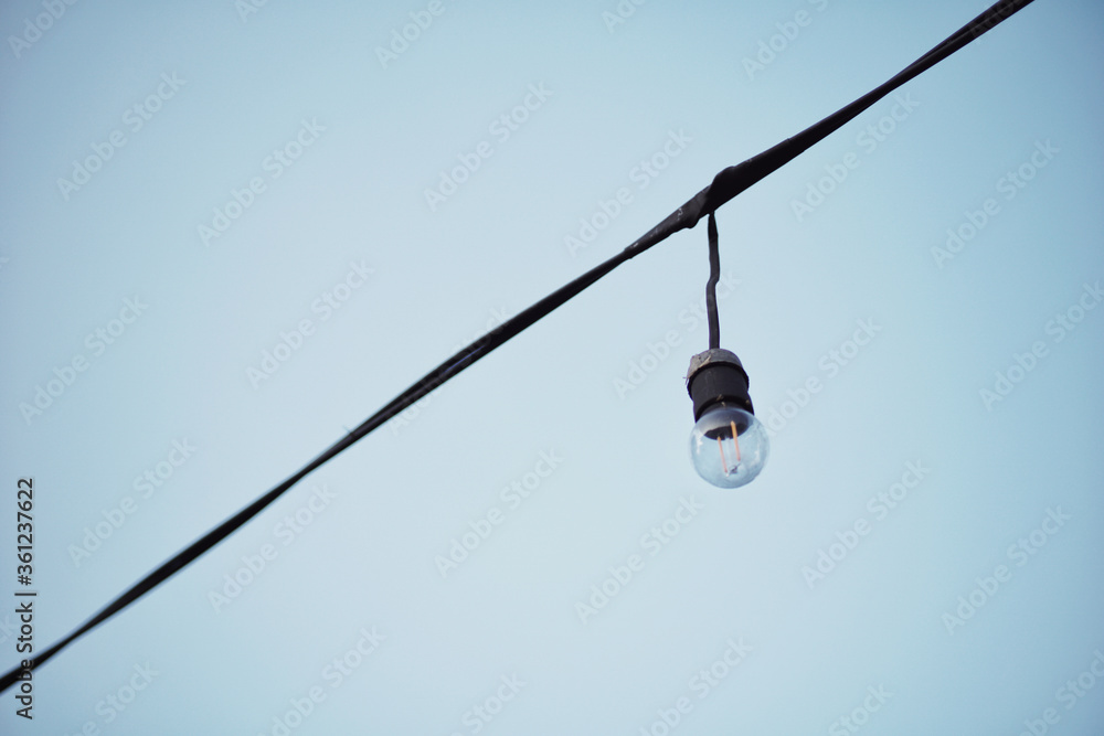 Light bulb hanging on a electricity wire with blue clear sky background ...