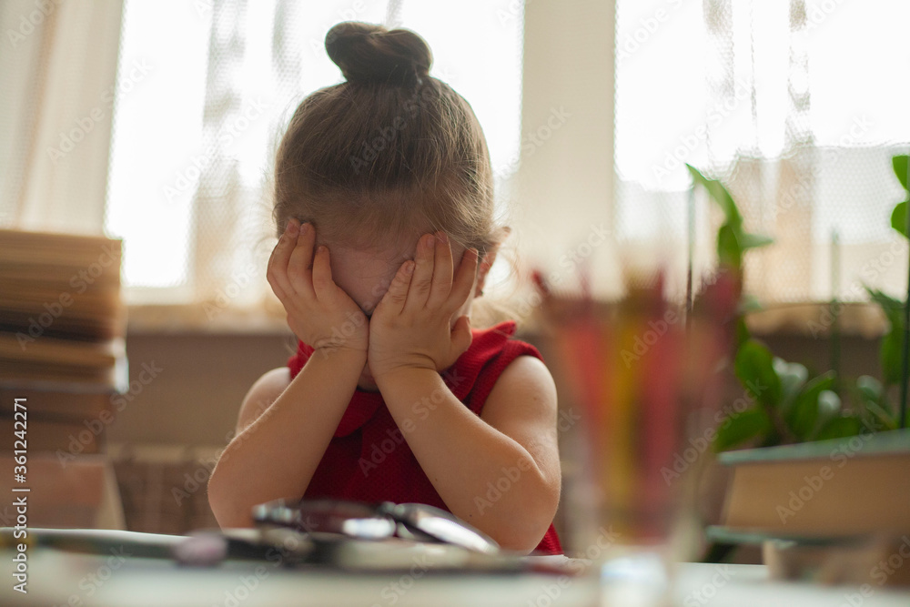 The little girl covered her face with her hands. The child is tired of ...