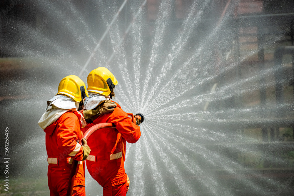 Two brave firefighter in fire suit on rescue duty using water from hose ...