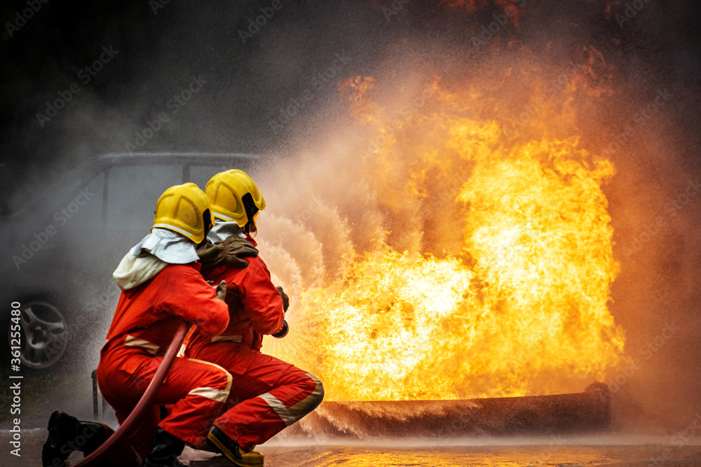Two brave firefighter in fire suit on rescue duty using water from hose ...