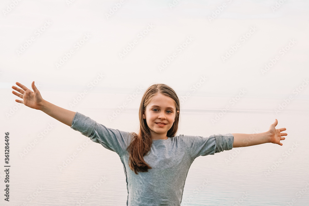 A happy little girl child stands with her arms outstretched against the ...