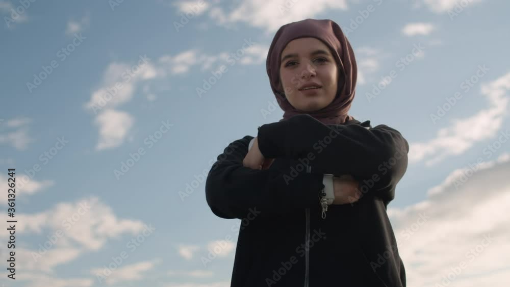A young Muslim woman in a hijab folds arms over her chest and looks ...