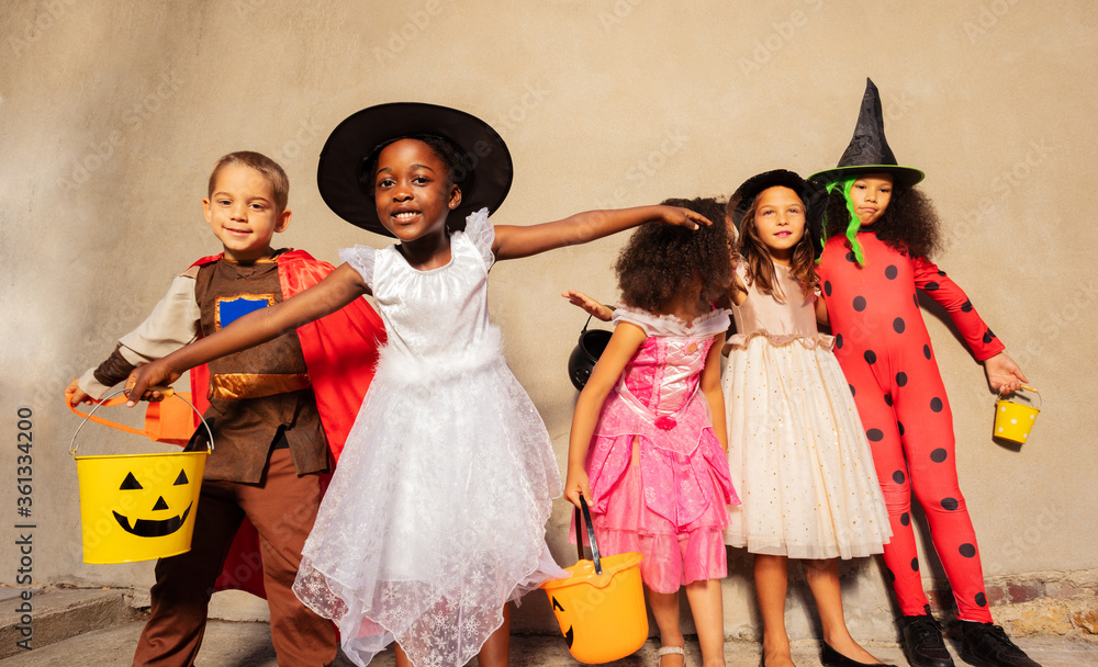 Girl with candy bucket over group of kids in Halloween costumes hug ...