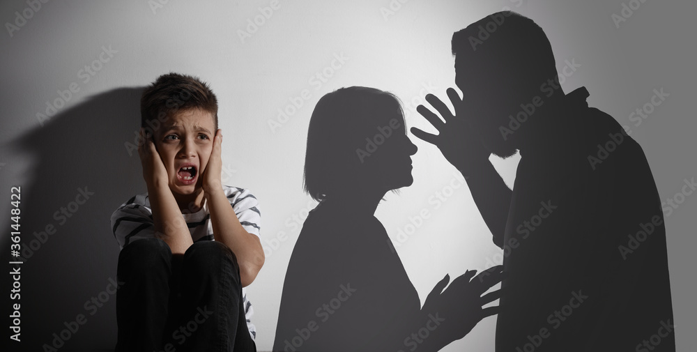 Scared little boy closing his ears and silhouettes of arguing parents ...