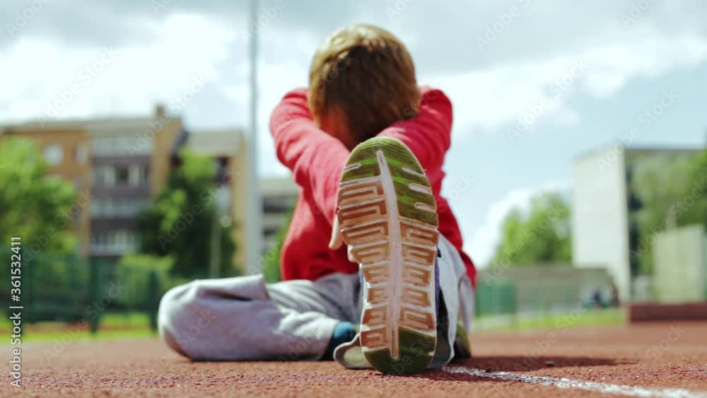 Preteen boy doing forward bends and stretching legs while sitting at ...