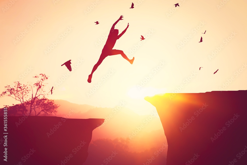 Silhouette man jumping between cliff at top of mountain background with ...
