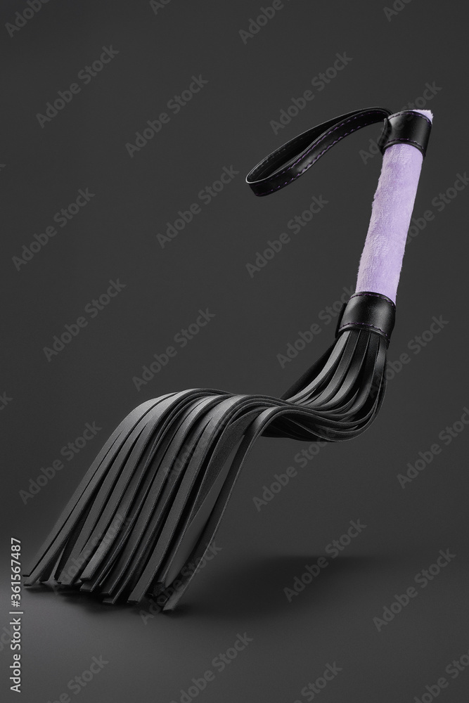 Detailed shot of a black whip with long leather fringe and violet plush ...