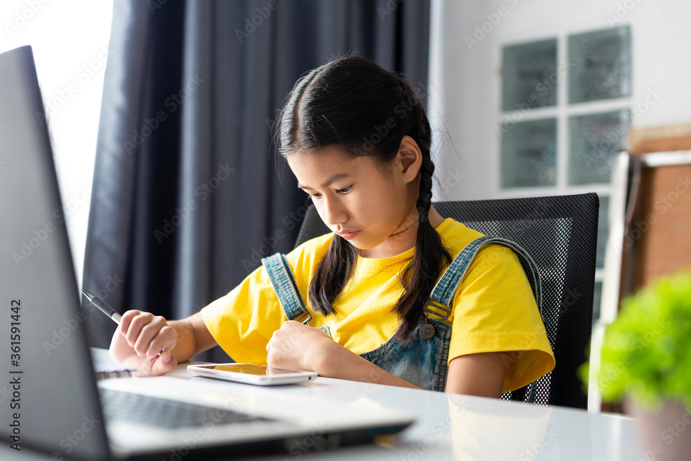 Cute Asian child girl uses smartphone in front of laptop computer at ...