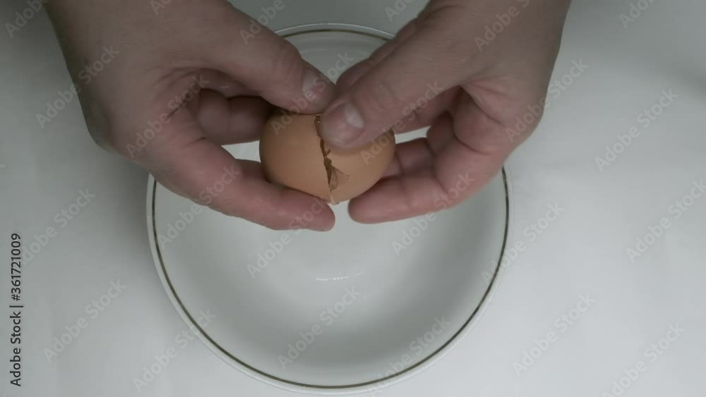 Top down view of female hands break white chicken egg and split yolk and egg white. Cooking at ...