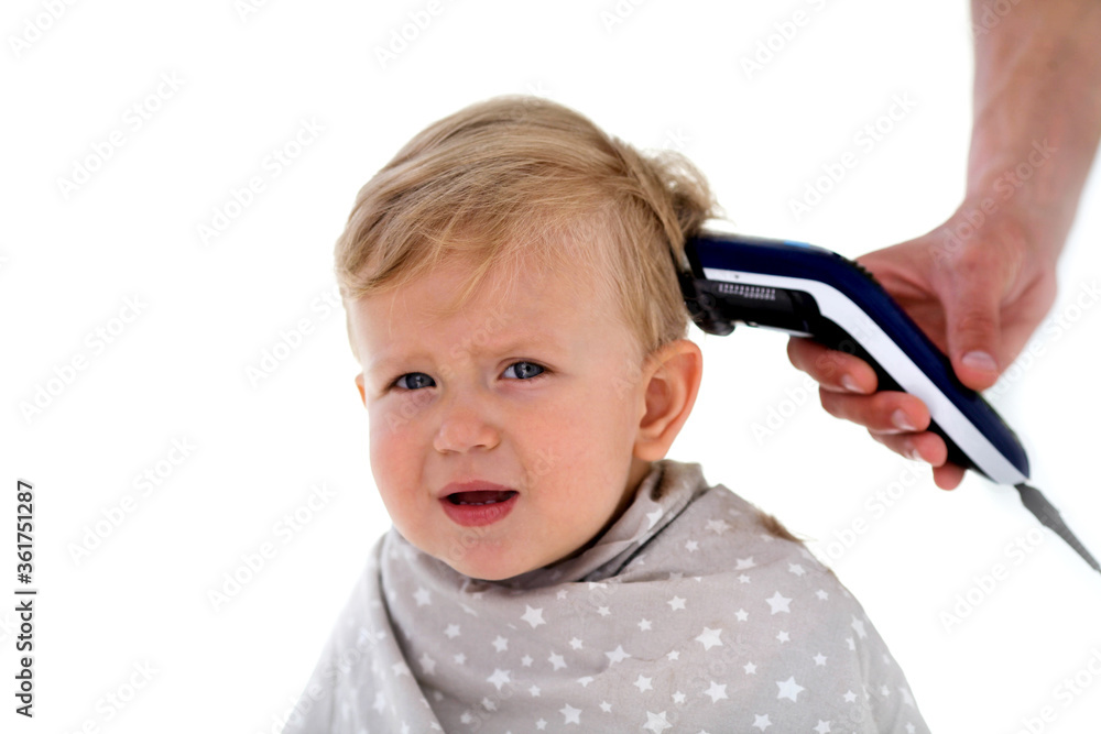 Female hands trim a crying baby with an electric hair clipper in a ...