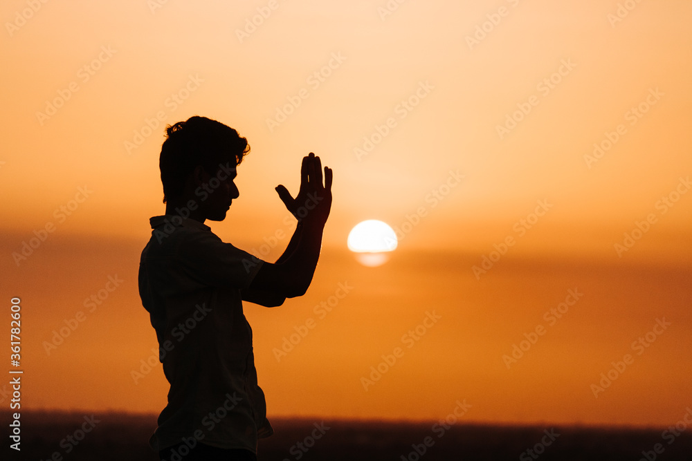 Silhouette of an Indian man praying in front of the sun during the ...