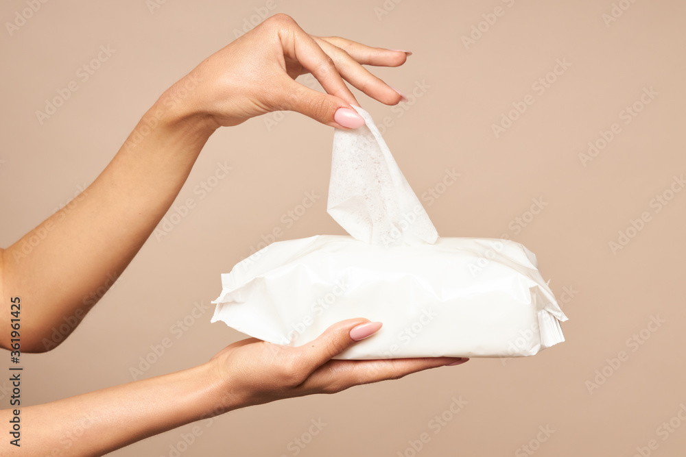 Hygiene. Female hands takes wet wipes from white packaging on a beige ...