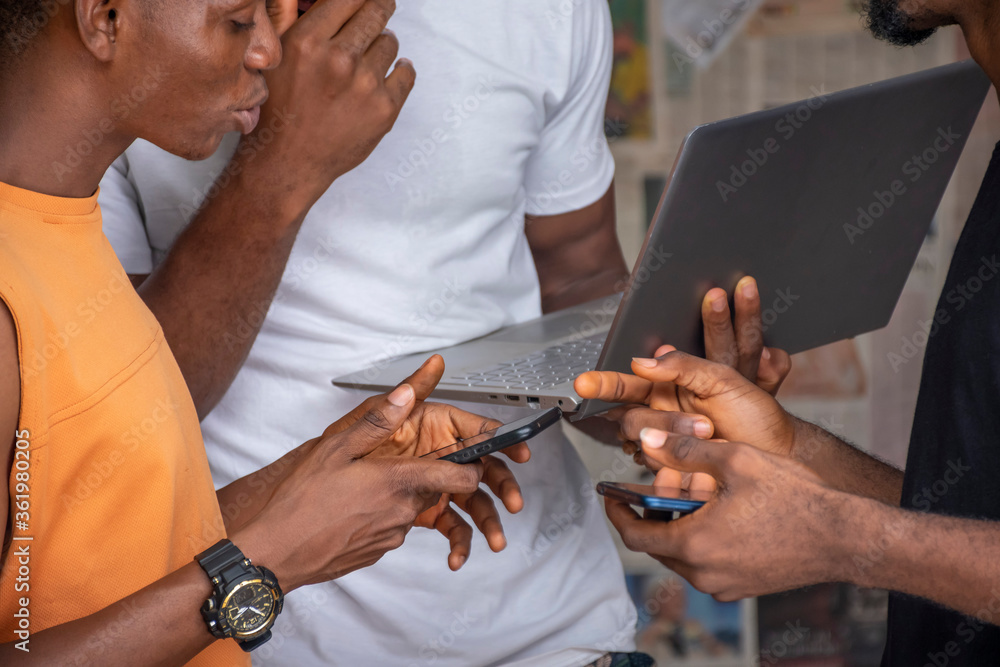 three young black people using their mobile phones and laptops, working ...