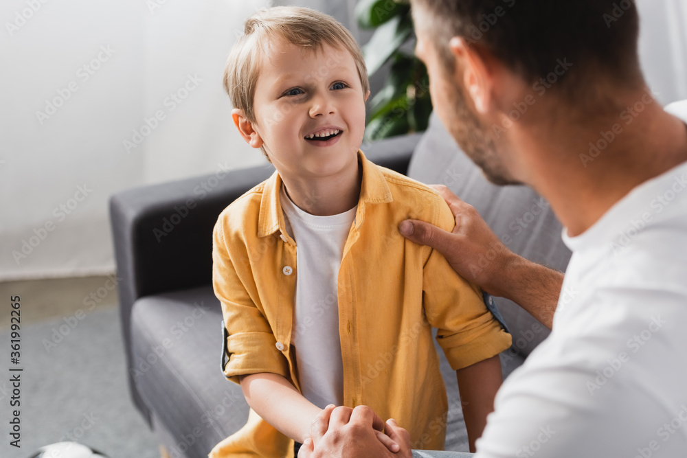selective focus of father touching shoulder and holding hand of smiling ...