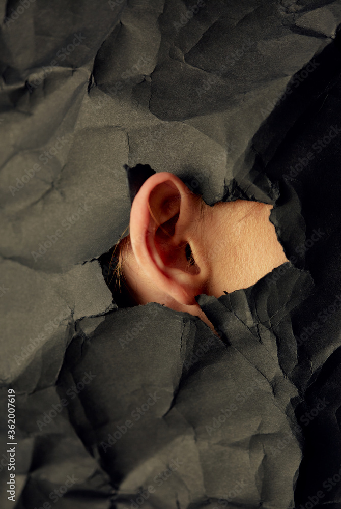 Woman's ear in hole in black crumpled paper background, black and white ...