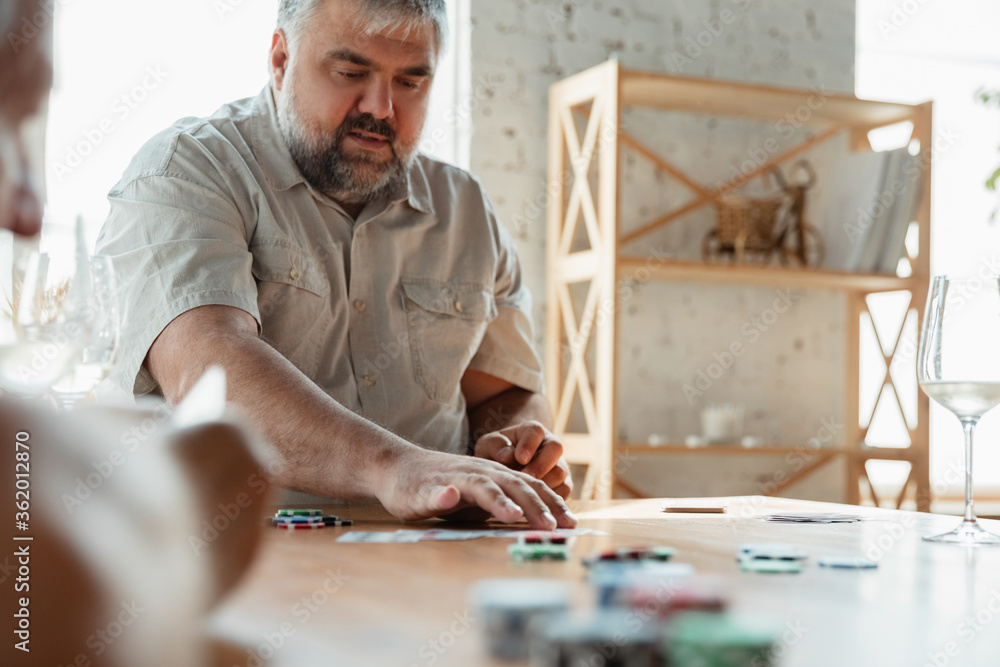 Shuffling. Two happy mature friends playing cards and drinking wine ...