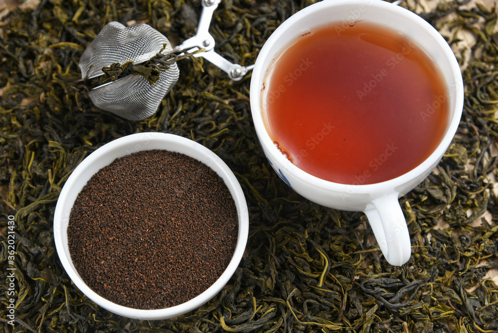 Cup of black tea and heap of dried organic tea leaves, dust and infuser ...