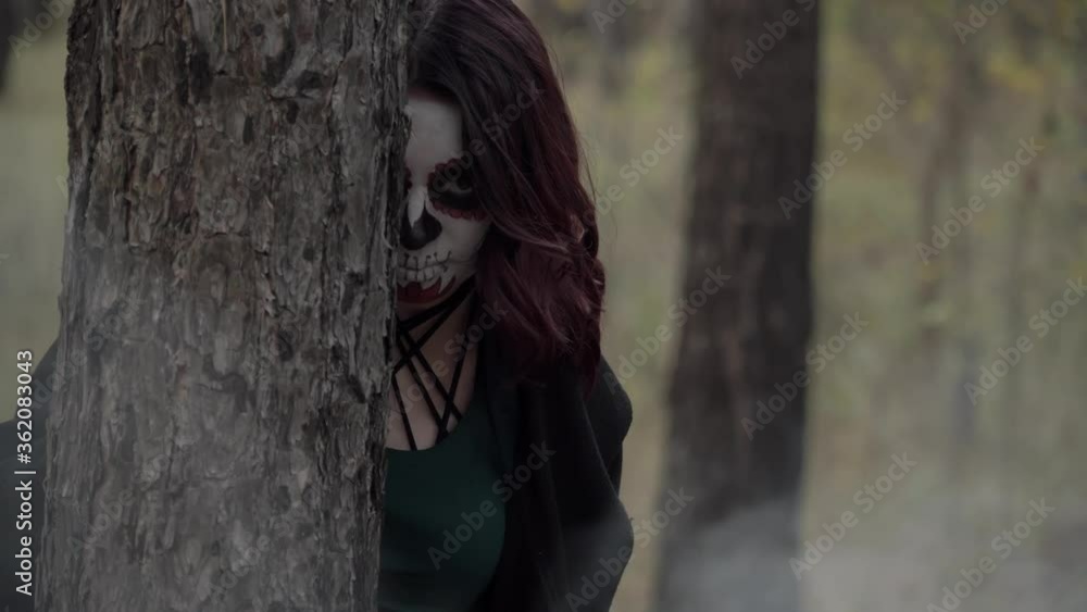Video Stock Witch with Santa Muerte makeup hides behind a tree in smoke ...